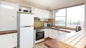 Cozinha com armários brancos, micro-ondas, forno e janela com vista para a cidade.