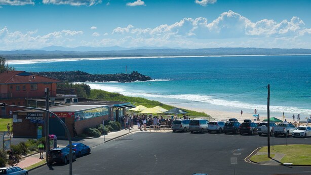 Vista costeira com praia, carros estacionados e um edifício com mural temático de praia.