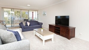Uma sala de estar com sofá, mesa de centro, rack para TV e porta de vidro deslizante para área externa.