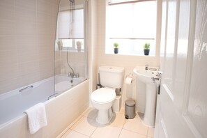 Uma casa de banho moderna com cabine de chuveiro em vidro, sanita, lavatório e janela com plantas em vasos.