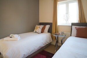 Quarto de hotel com duas camas, uma mesa pequena com uma chávena e um prato, e uma janela com cortinas.