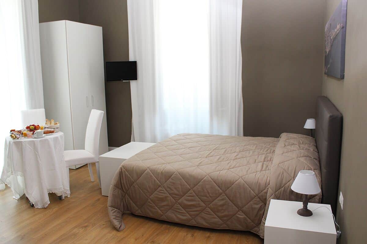 Quarto com cama, mesa de cabeceira, cadeira e uma pequena mesa com petiscos.