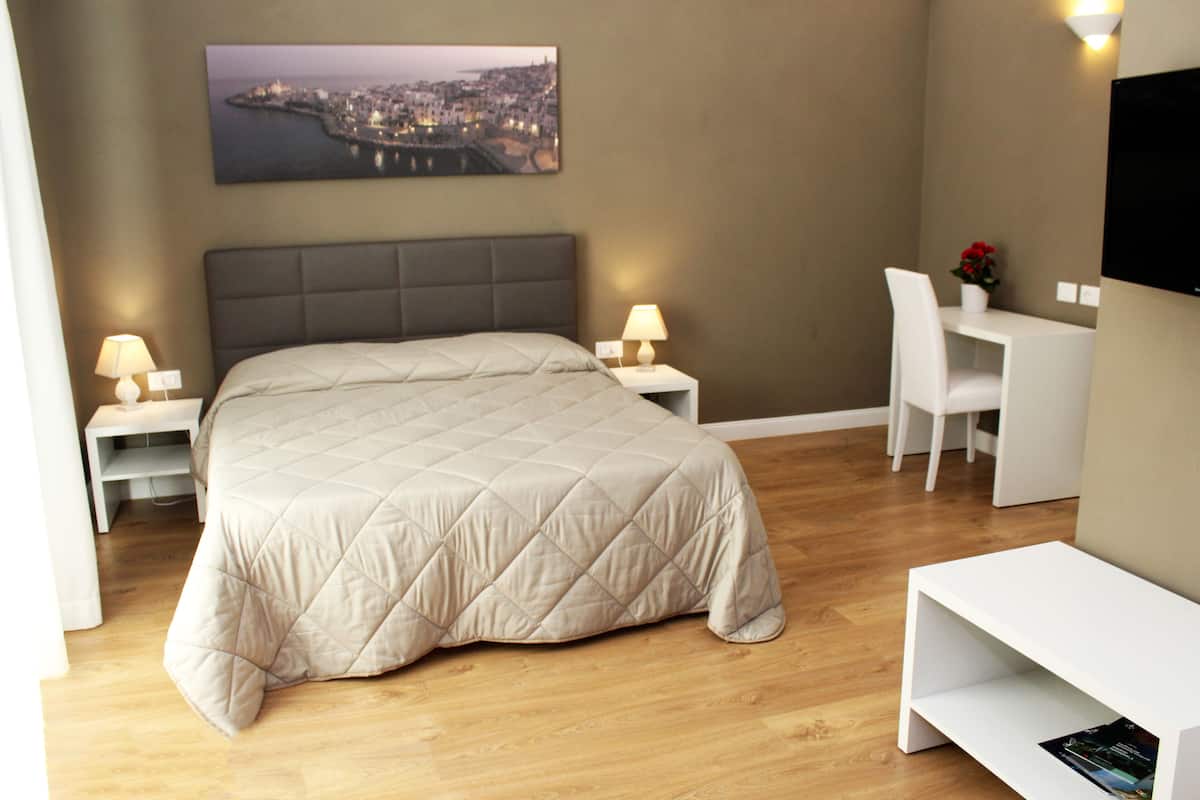 Quarto com uma cama grande, mesas de cabeceira com luminárias, uma escrivaninha com cadeira e uma televisão de tela plana na parede.