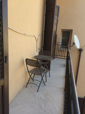 Um pequeno pátio externo com uma mesa redonda e duas cadeiras, uma antena parabólica e uma porta com persianas.