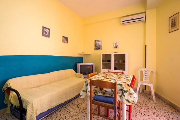 Quarto com sofá, mesa com toalha de mesa florida, televisão e armário.