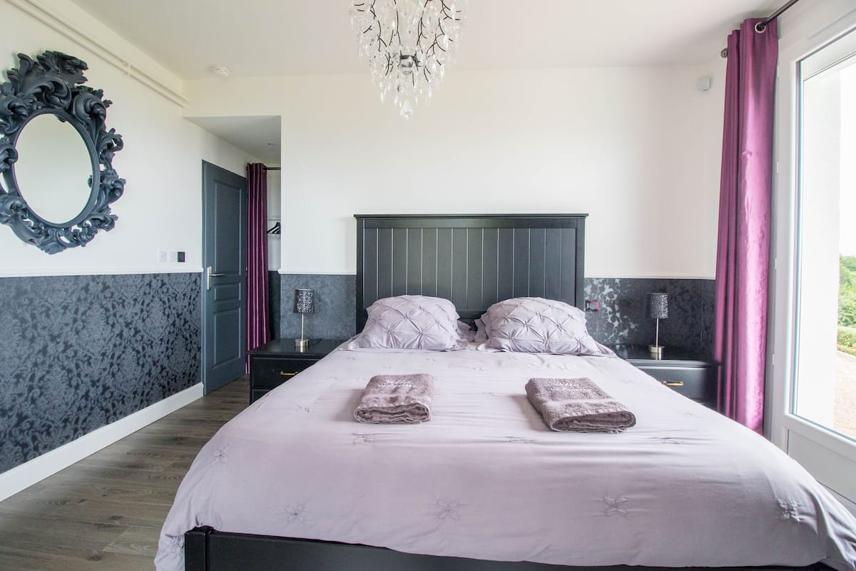 Quarto com cama grande, um lustre, um espelho e vista para o exterior.