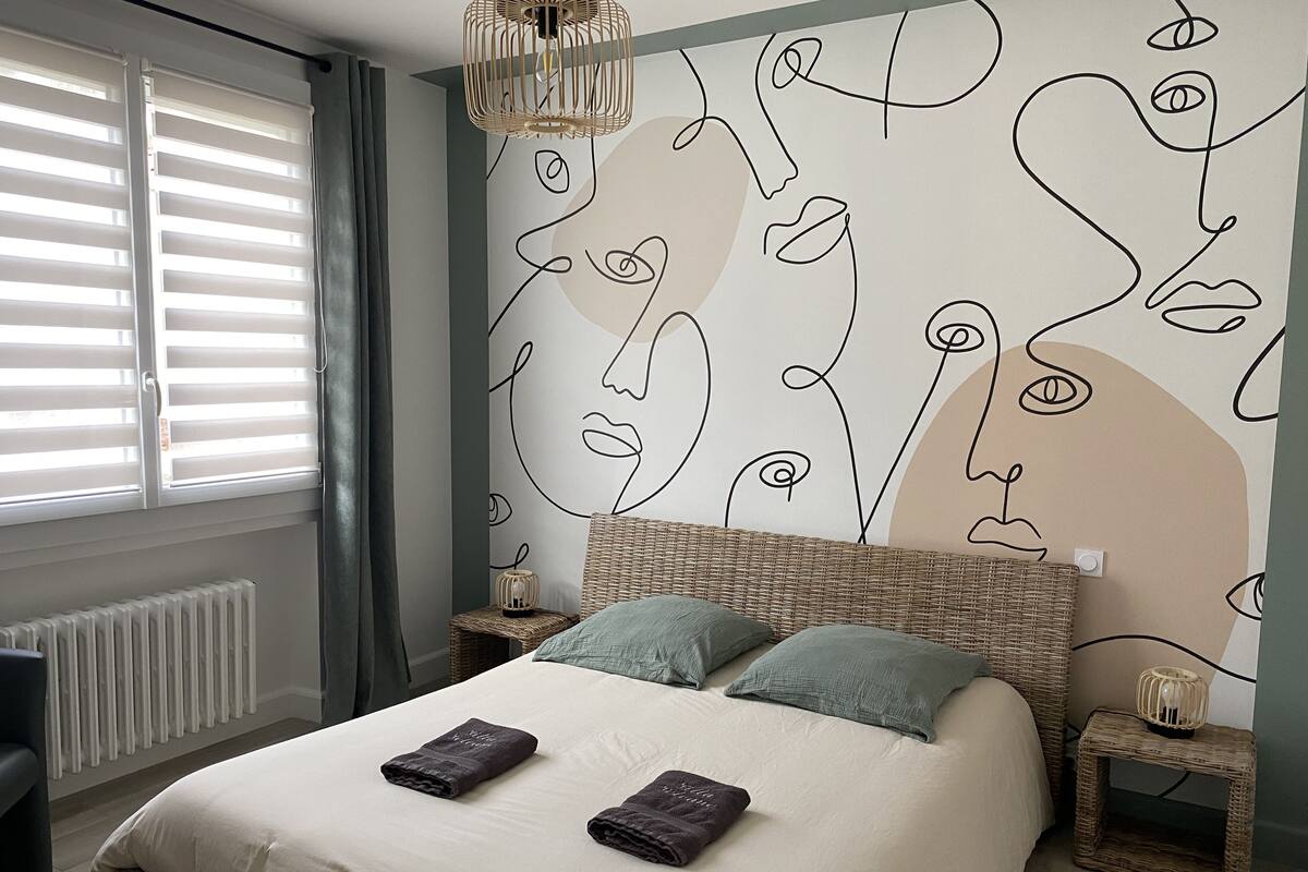 Quarto com uma cama grande, duas mesas de cabeceira, um painel de cabeça em vime e uma parede com arte abstrata em linhas.