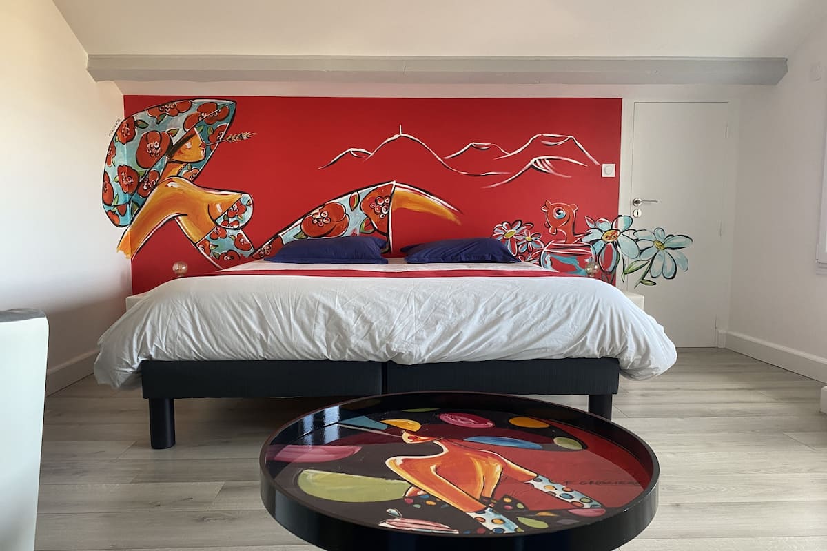 Quarto com cama, mesa redonda e um mural colorido na parede.