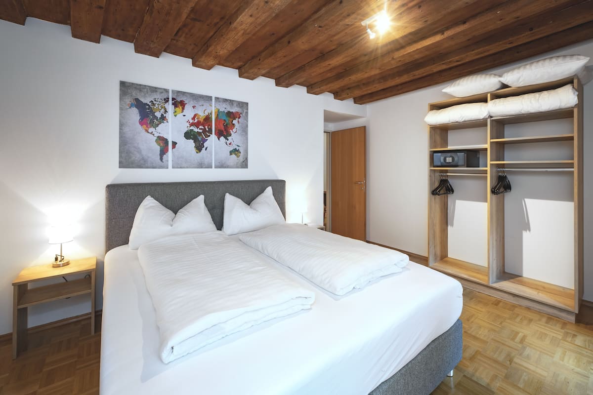 Uma cama bem arrumada com lençóis brancos, cabeceira de madeira e uma obra de arte com um mapa-múndi acima.