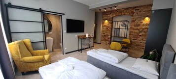 Quarto de hotel moderno com porta deslizante, TV de tela plana, parede de tijolos, mesa pequena e sofá.