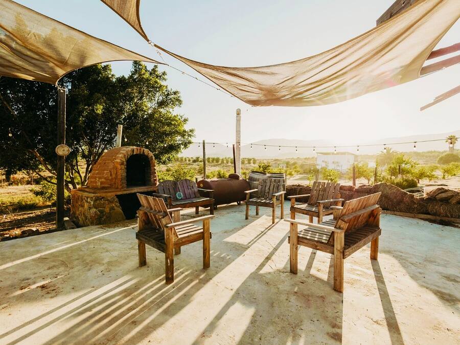 Um pátio ao ar livre com forno de tijolos, cadeiras de madeira e uma mesa.