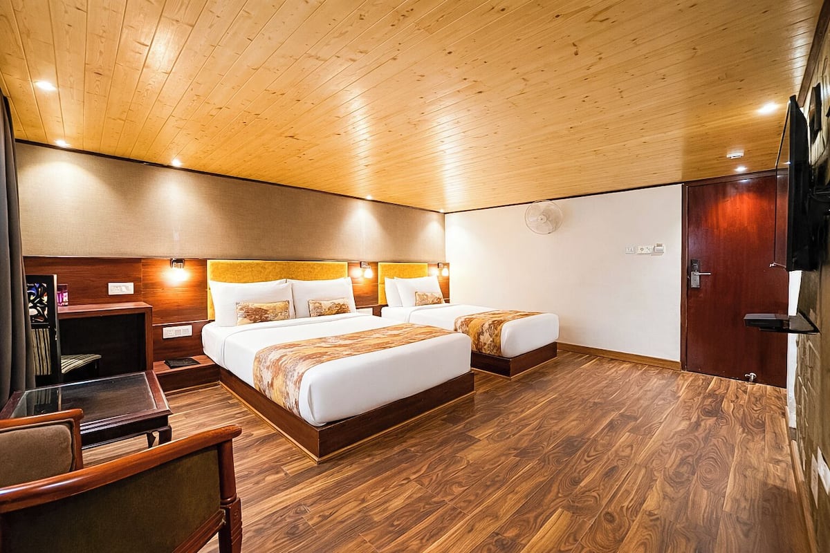 Quarto de hotel com teto de madeira, duas camas com roupa de cama branca, mesa de cabeceira de madeira, uma cadeira e uma televisão.