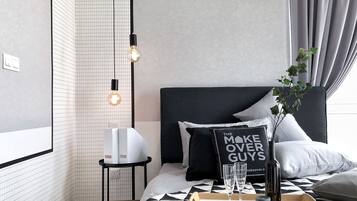 Um quarto moderno com um edredom estampado com padrão geométrico, uma mesinha de cabeceira com uma garrafa e copos, e um aplique na parede.