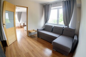 Uma sala de estar moderna com um sofá cinzento, soalho de madeira, uma mesinha e uma janela com cortinas.