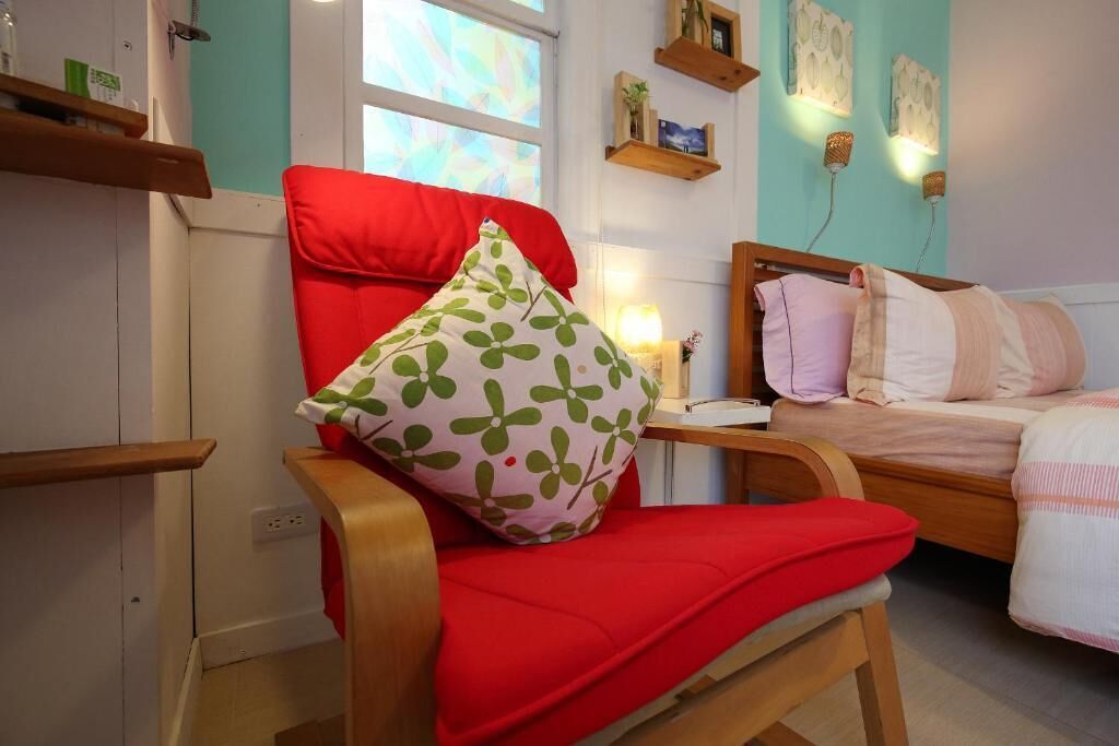 Um quarto aconchegante com uma cadeira de madeira, uma cama com manta listrada em rosa e branco, e uma janela com vista para o céu.