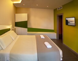 Quarto de hotel com cama, guarda-roupa, um banco e televisão na parede.