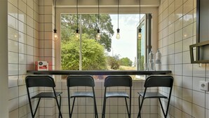 Uma cozinha com três banquetas, uma janela com vista para vegetação e lâmpadas penduradas.