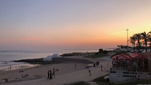 Um calçadão costeiro com uma praia, palmeiras e um restaurante Super Rock.