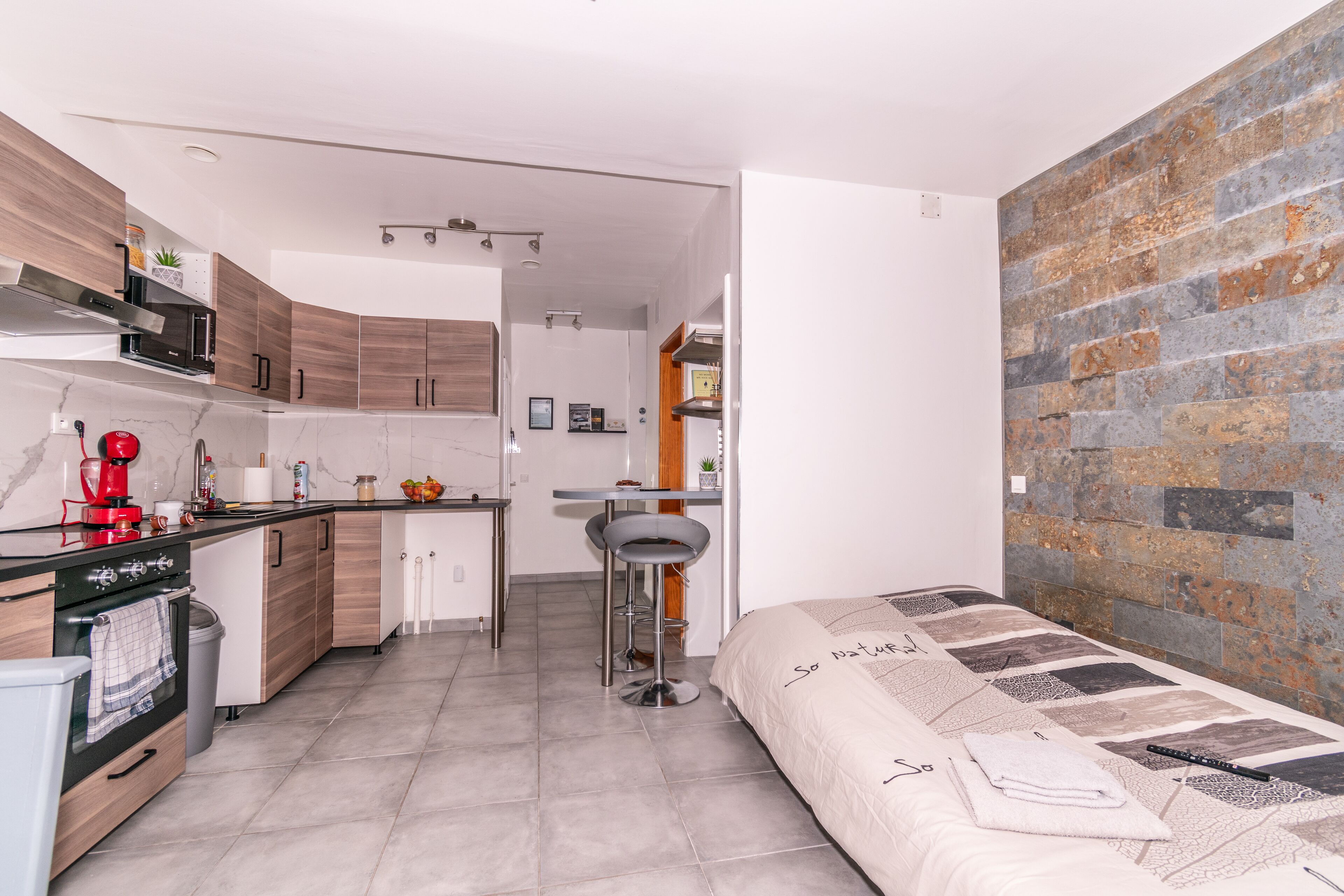 Cozinha compacta com eletrodomésticos modernos, área de jantar e cama com colcha.