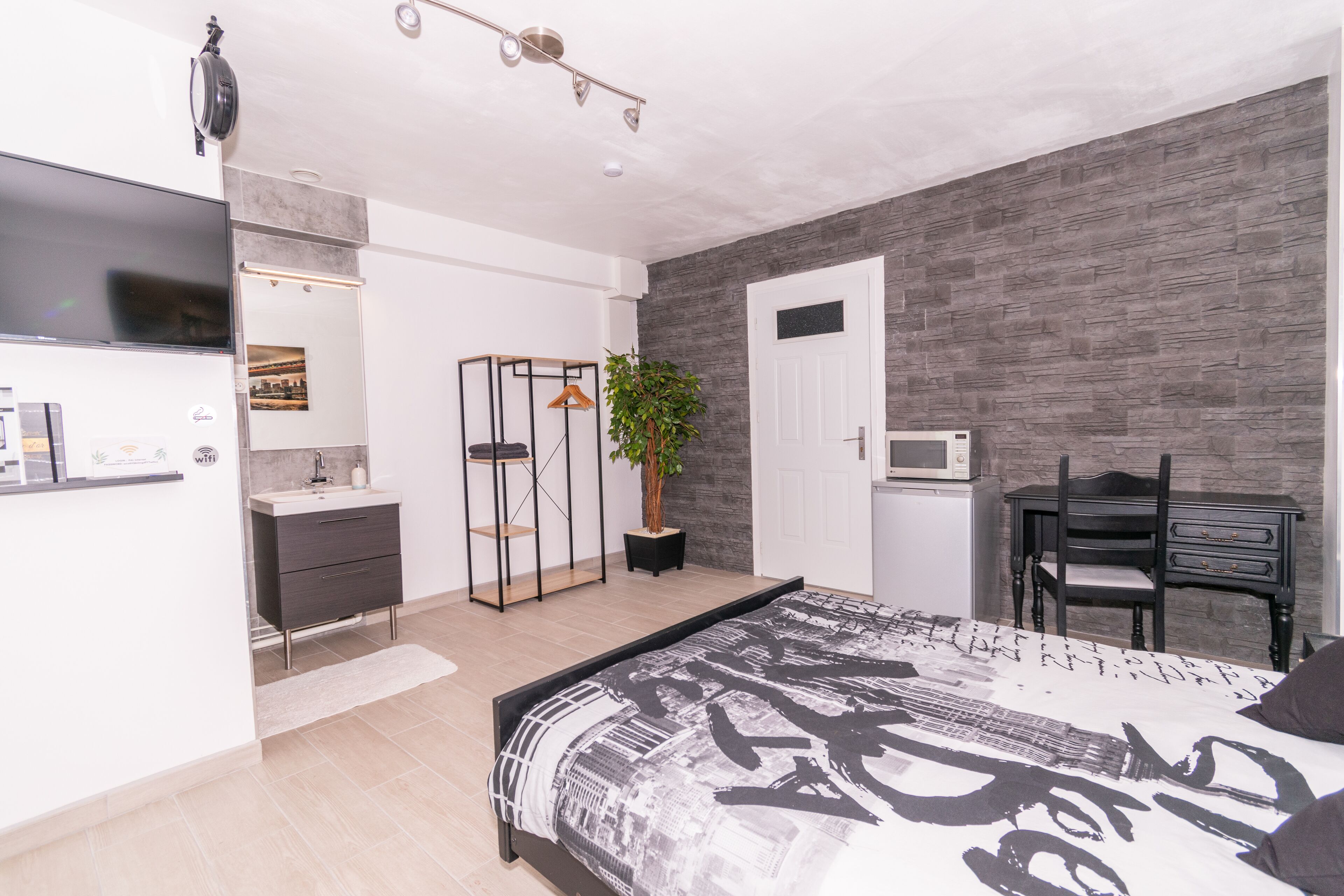 Quarto moderno com cama, escrivaninha, cadeira, planta e banheiro.