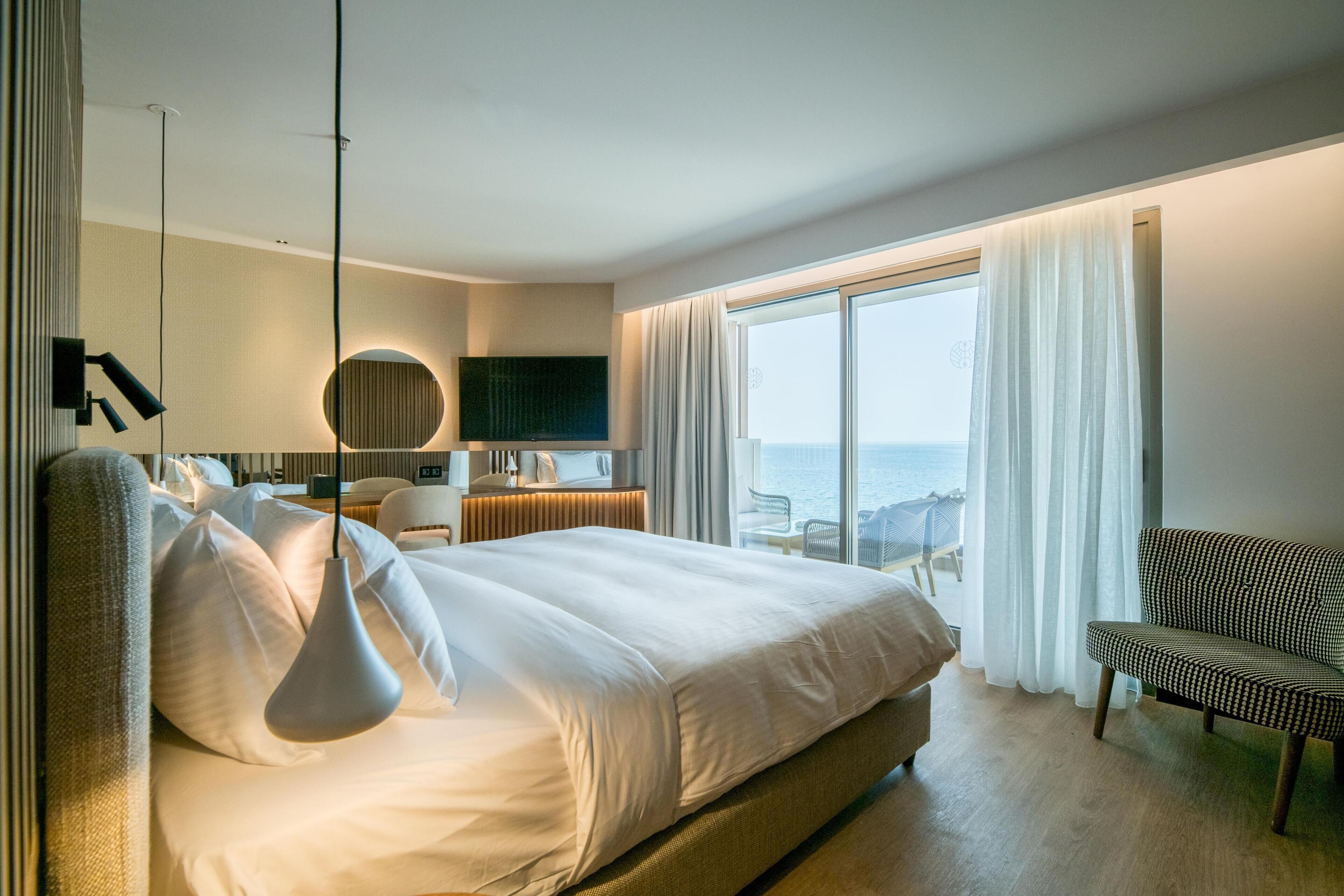 Quarto de hotel com uma cama grande, uma mesa, uma cadeira e vista para o mar.