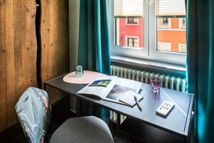 Quarto com parede de madeira, janela com cortinas, mesa com revista, um copo e um controle remoto.