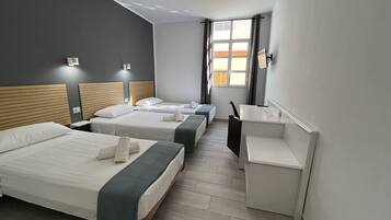 Quarto de hotel com três camas, uma mesa e uma janela com cortinas.