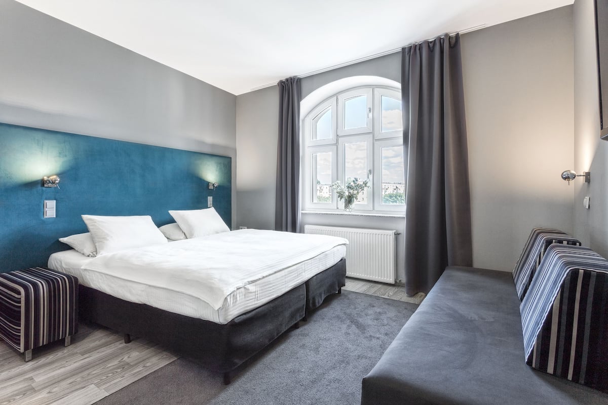 Quarto moderno com uma cama grande, um banquinho e uma janela com cortinas.