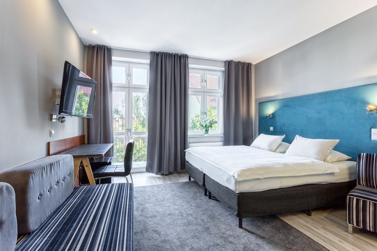 Quarto de hotel com cama, escrivaninha, cadeira, televisão e vista para o exterior.