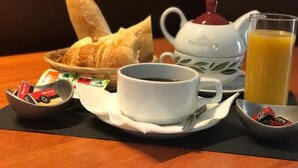 Uma mesa de café da manhã com croissants, um bule, uma xícara de café, um copo de suco de laranja e uma tigela com sachês de chá.