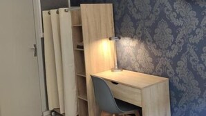 Quarto compacto com escrivaninha, cadeira e televisão na parede.
