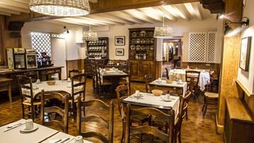 Um restaurante acolhedor com mobiliário de madeira e ambiente agradável, com mesas preparadas para refeições e uma vitrine de pratos em prateleiras.