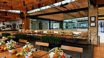 Um restaurante com mesas de madeira, centros de mesa com flores e um teto alto com vigas aparentes.