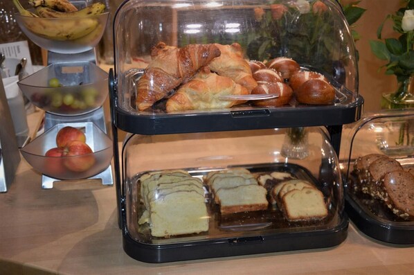 Buffet com diversos alimentos, incluindo croissants, pão e doces.