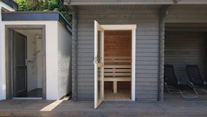 Uma área externa coberta com um banco de madeira, uma porta que dá para um chuveiro e um espaço de estar com cadeiras.
