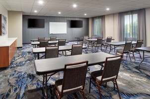 Uma sala de conferências com uma mesa grande, várias cadeiras, um quadro branco, uma televisão e piso coberto de carpete.