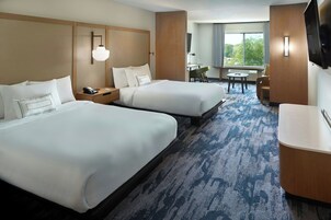 Quarto de hotel com duas camas, uma escrivaninha, uma cadeira, uma televisão e janela com vista para árvores.