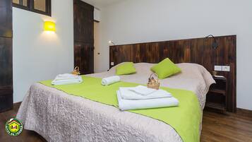 Quarto de hotel com cama grande, roupa de cama verde e cabeceira de madeira. Há toalhas e uma cesta na cama.