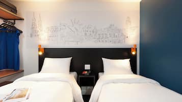 Quarto de hotel com duas camas, uma mesa de cabeceira com abajur, uma pintura urbana na parede e uma parede azul decorativa.