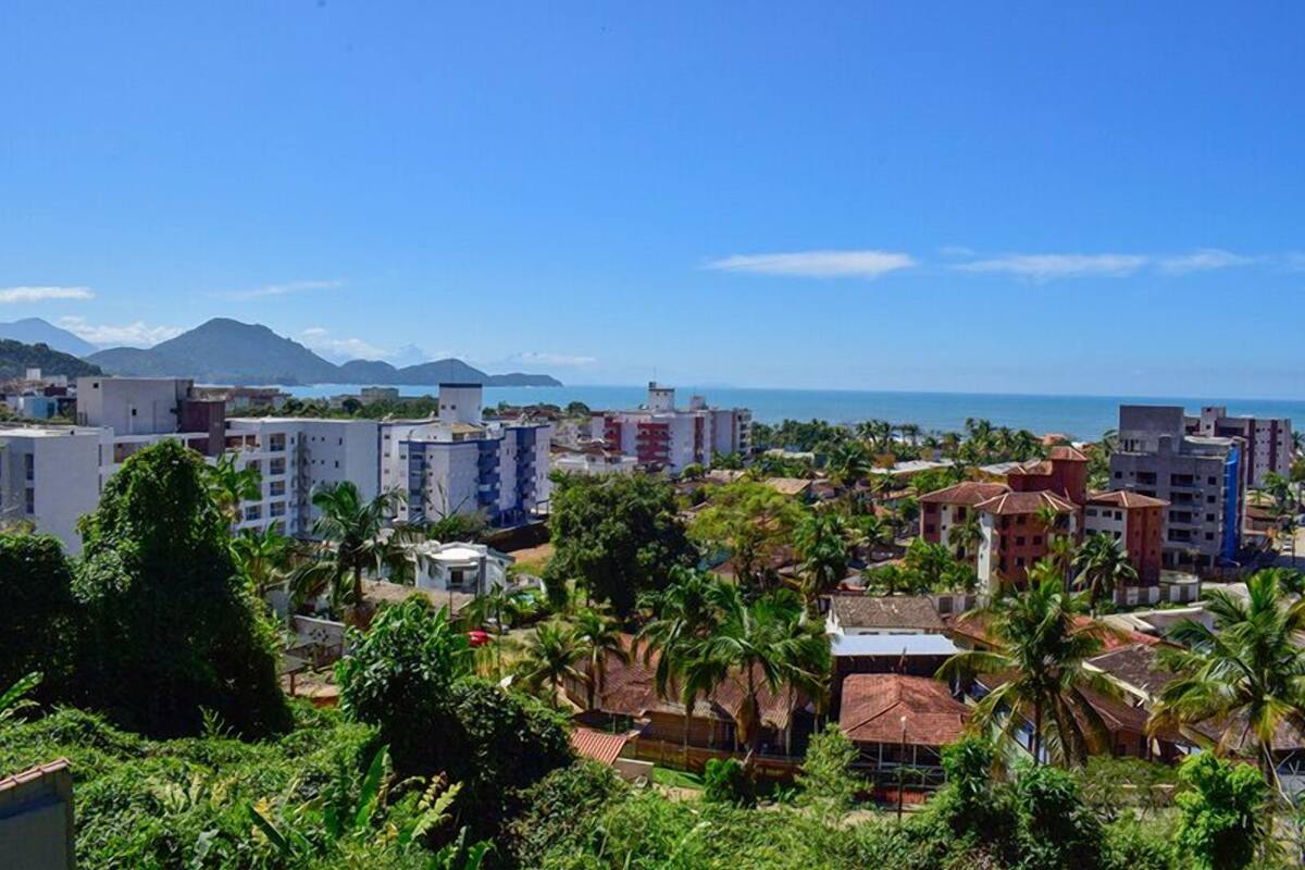 Paisagem costeira com uma mistura de edifícios residenciais e comerciais, céu azul límpido e uma cordilheira distante.