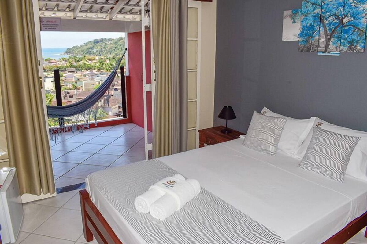 Quarto de hotel com cama, mesa de cabeceira, luminária, vista para uma rede e paisagem cênica.