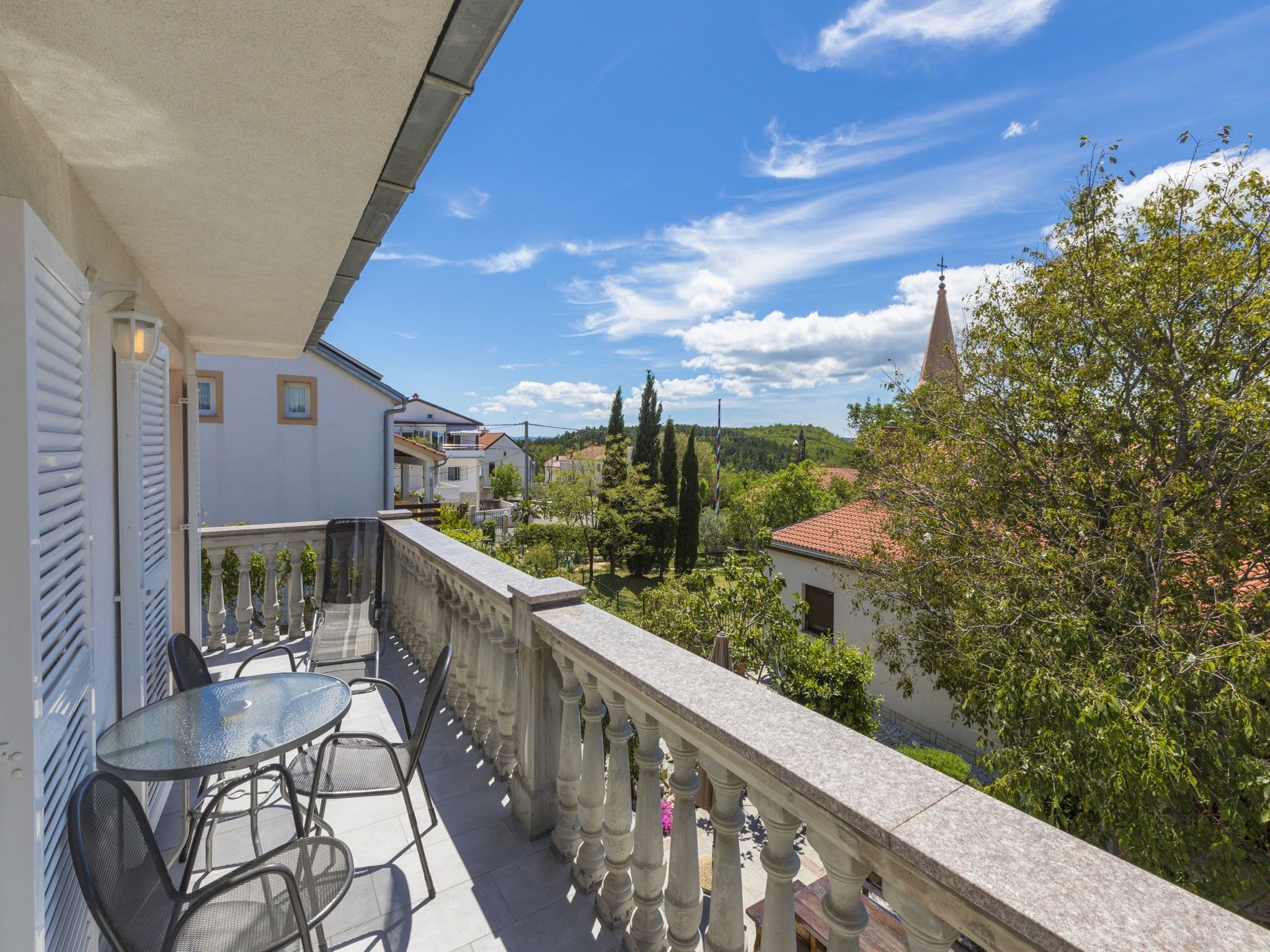 Uma varanda com mesa e cadeiras, com vista para uma cidade com edifícios e uma igreja.