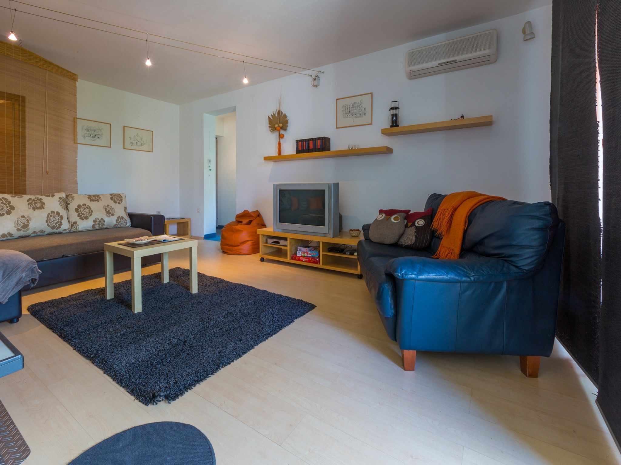 Uma sala de estar com sofá, poltrona azul, televisão e uma mesinha.