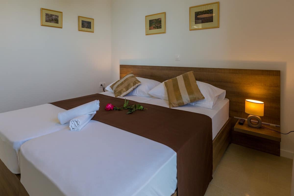 Quarto de hotel com duas camas, uma mesinha de cabeceira com abajur e três quadros na parede.