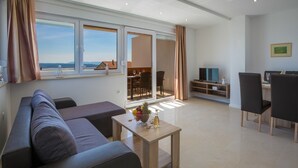 Uma sala de estar moderna com um sofá, uma mesa de centro com frutas e uma garrafa, uma televisão e uma área de jantar com cadeiras e uma mesa.