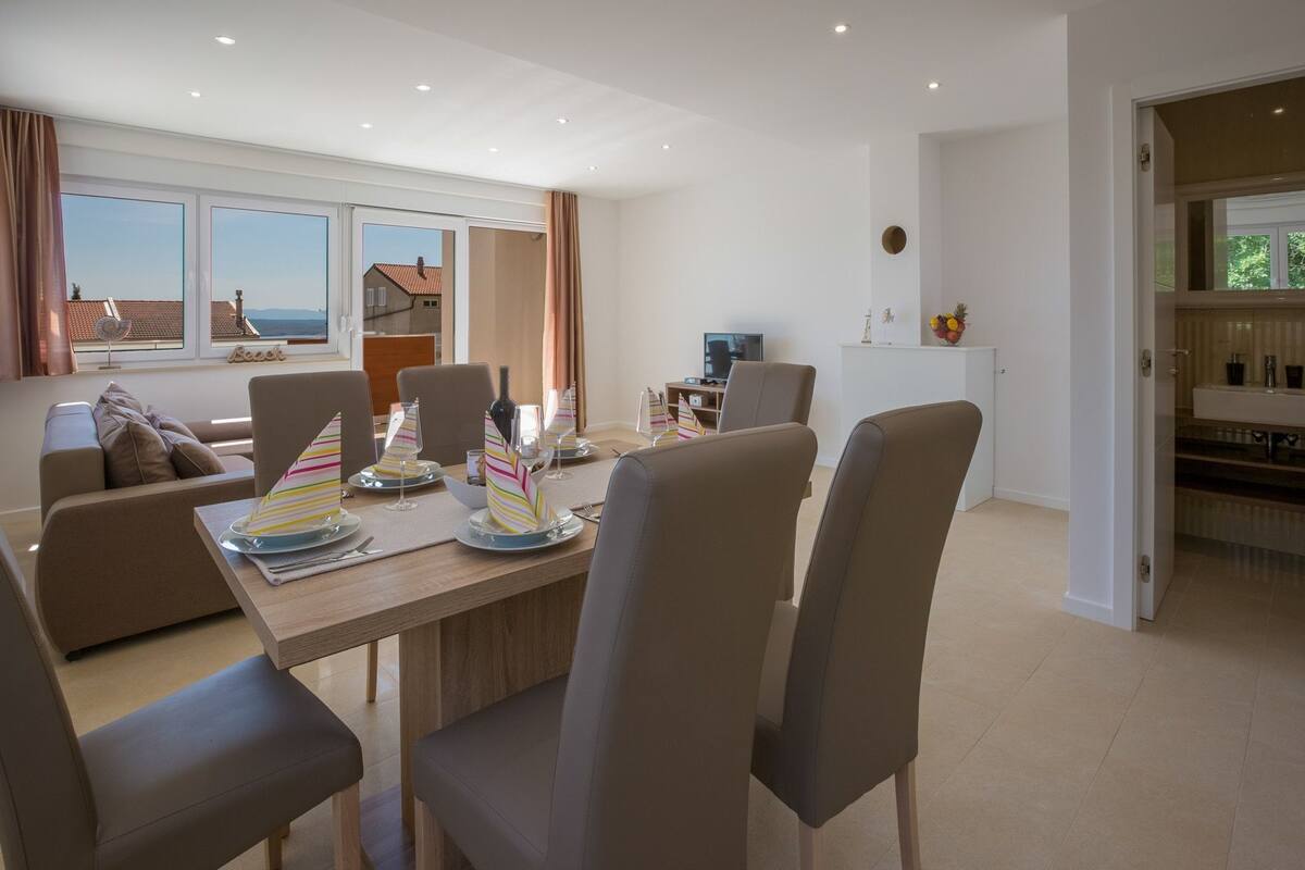 Uma sala de jantar moderna com uma mesa de madeira posta para seis pessoas, rodeada por seis cadeiras.