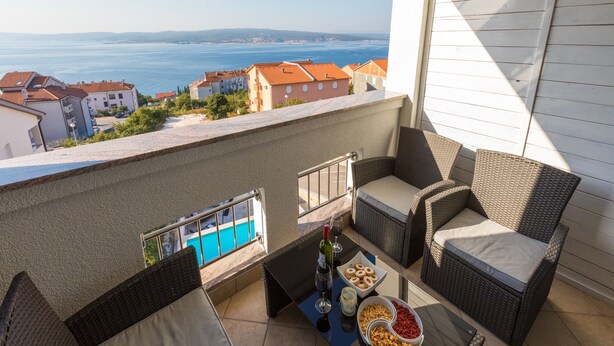 Uma varanda com mobiliário de vime, piscina e vista para o mar e edifícios.