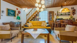 Uma sala de estar com sofá, duas poltronas, uma mesa de centro, escadas, uma área de cozinha e uma mesa de jantar.