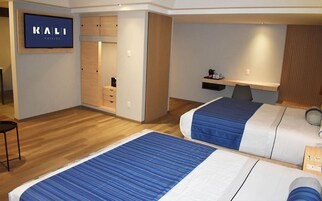 Quarto de hotel com duas camas, televisão, guarda-roupa e secretária com cadeira.