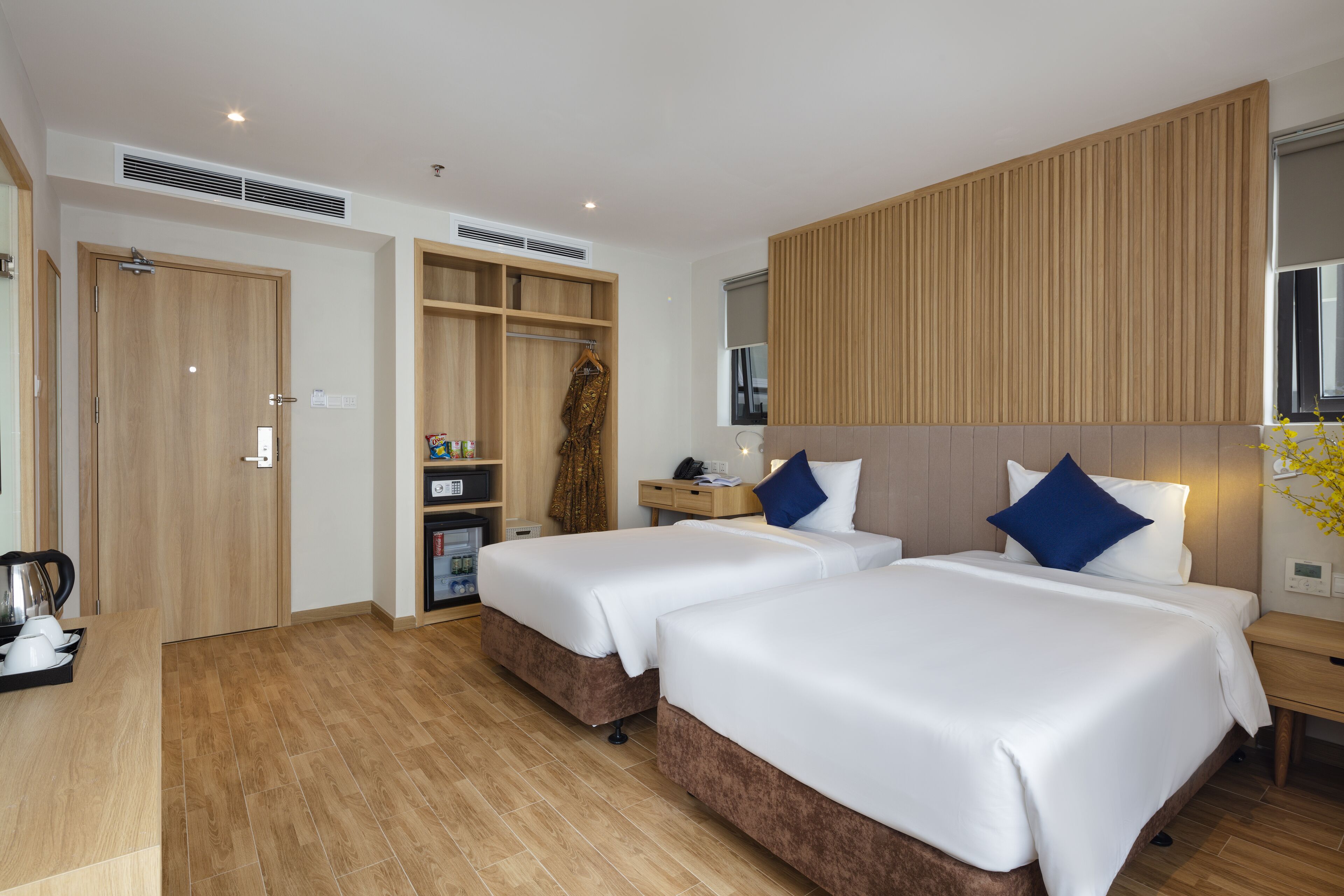 Quarto de hotel com duas camas, um guarda-roupa, uma mesa de trabalho e um banheiro.